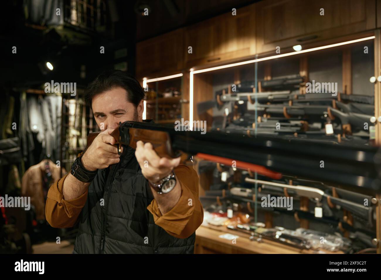Weapon shop owner aiming with gun while standing over showcase gun rack ...