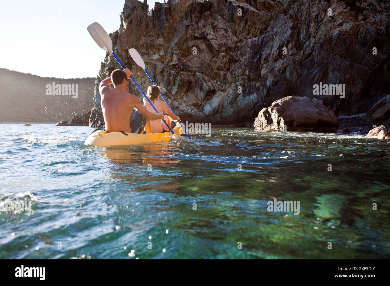 A back-lit man and a woman kayak into a rocky cove on the island of St ...