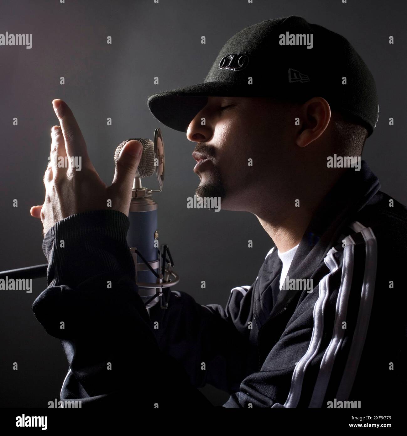 A hispanic rapper, wearing urban street clothes, sings into a ...