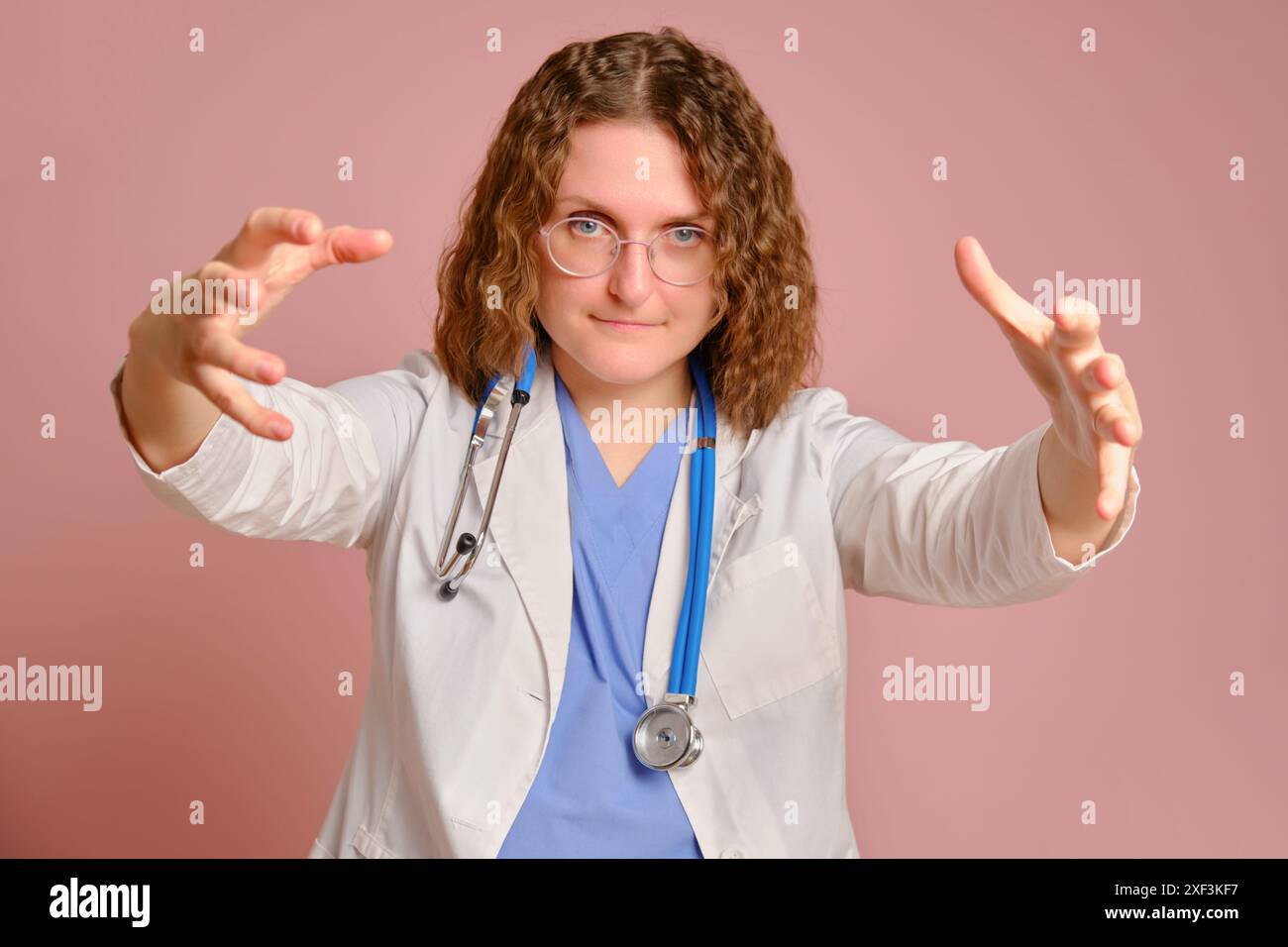 Woman doctor reaching out with her hands to a patient, studio pink ...