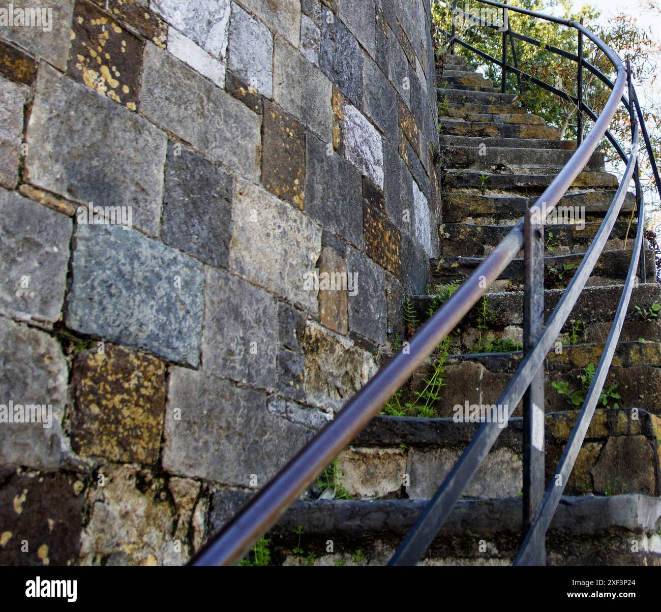 An old stone staircase rises alongside a weathered brick wall, with greenery peeking through the ...