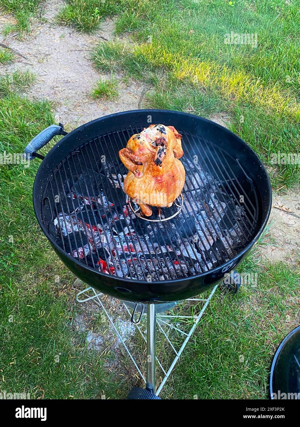 A whole chicken is being roasted over hot coals on a charcoal grill in ...