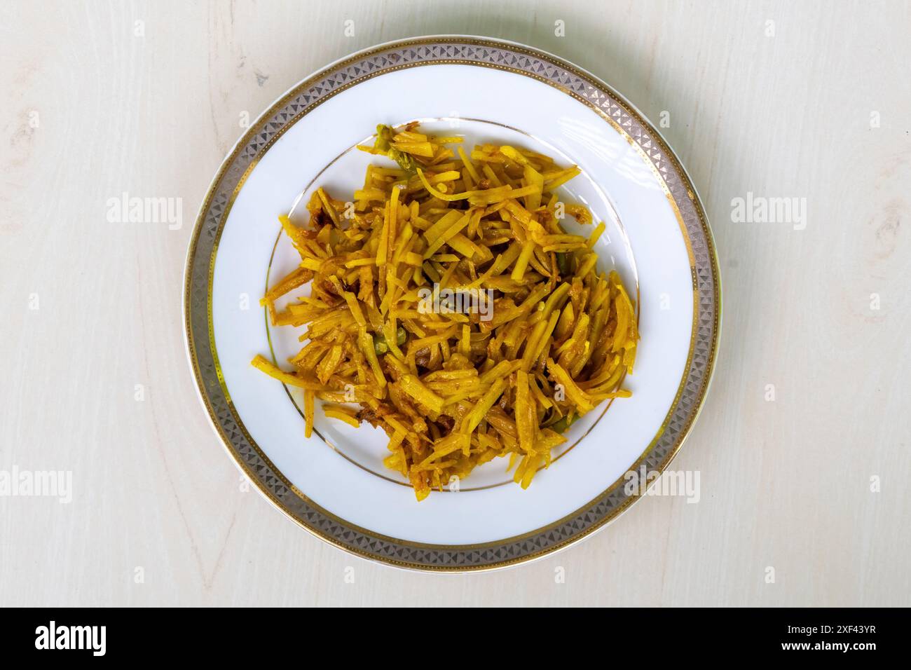 Aloo bhaji or fried grated potato in a white plate on wooden background ...