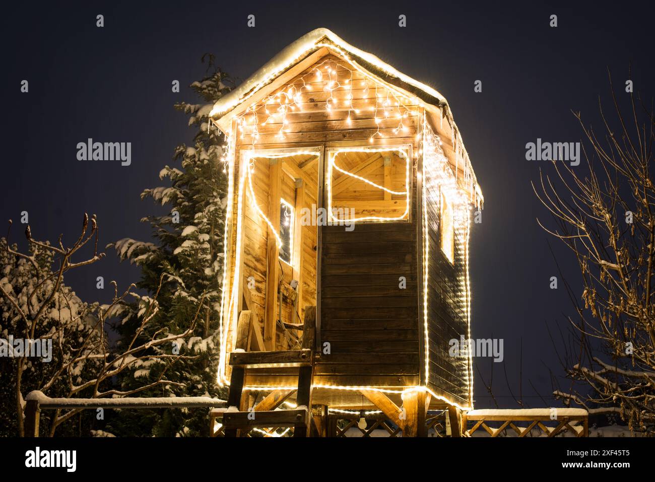 A wooden treehouse on a winter night - covered in snow and lit up with ...