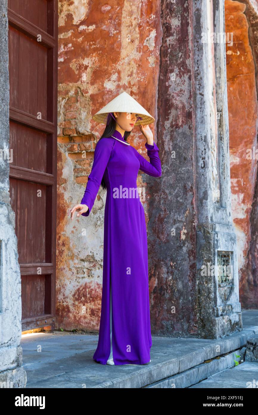 Pretty Vietnamese young woman wearing traditional Ao Dai tunic and conical hat at Minh Mang King ...