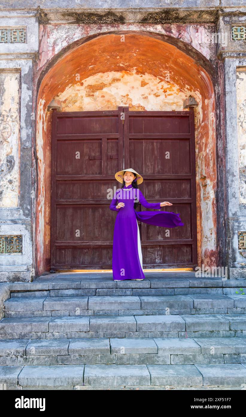 Pretty Vietnamese young woman wearing traditional Ao Dai tunic and conical hat at Minh Mang King ...