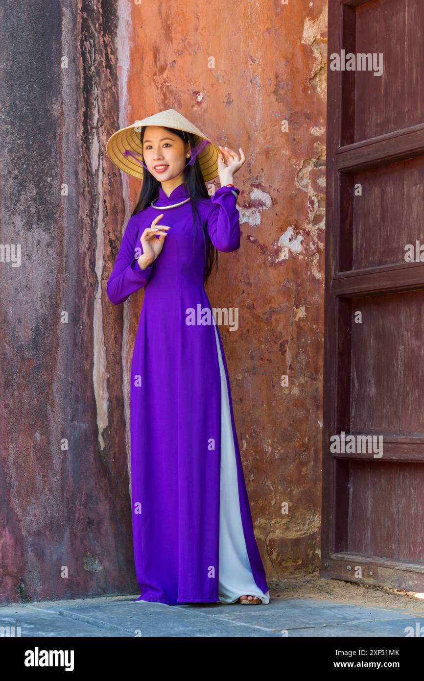 Pretty Vietnamese young woman wearing traditional Ao Dai tunic and conical hat at Minh Mang King ...