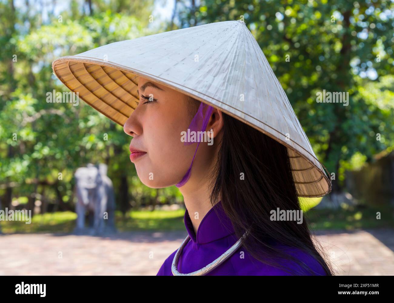 Pretty Vietnamese young woman wearing traditional Ao Dai tunic and conical hat at Minh Mang King ...