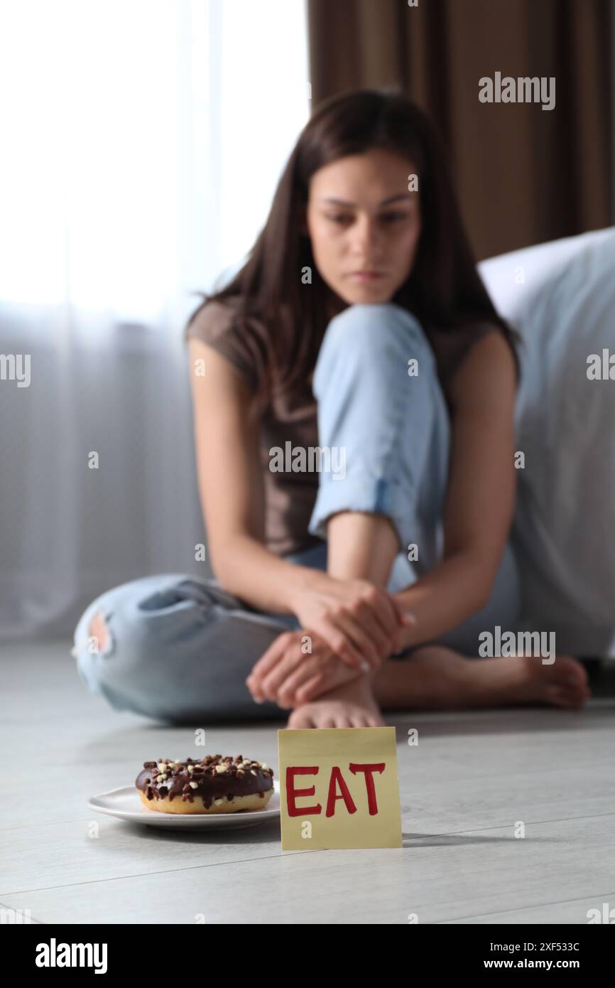 Eating disorder. Sad woman sitting on floor indoors, focus on note with ...