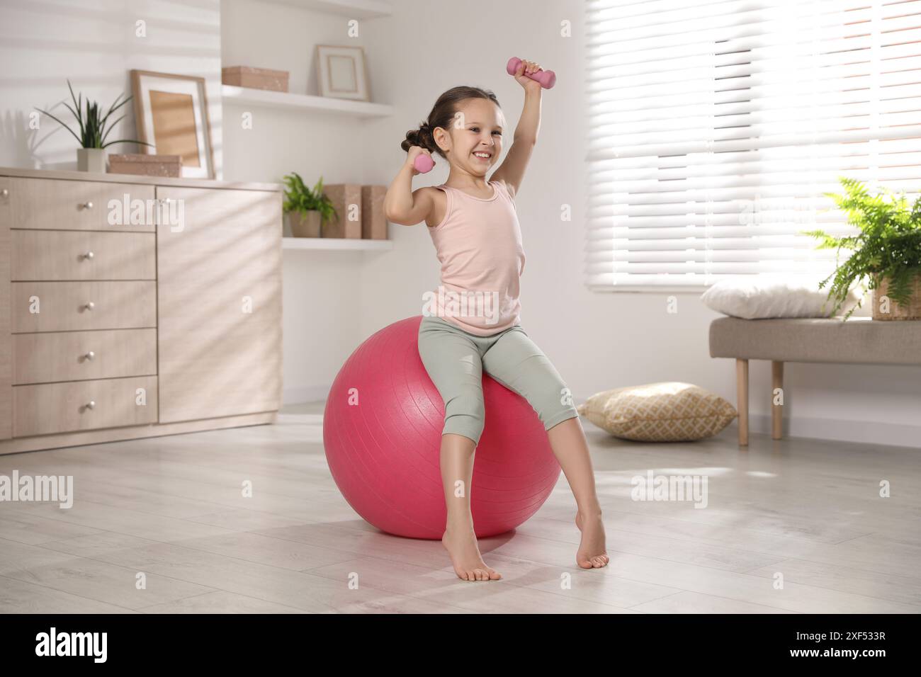 Cute little girl doing exercises with dumbbells and fit ball at home ...