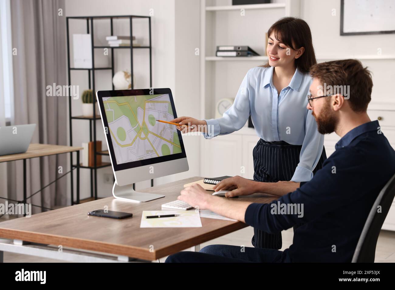 Cartographers working with cadastral map on computer at table in office ...