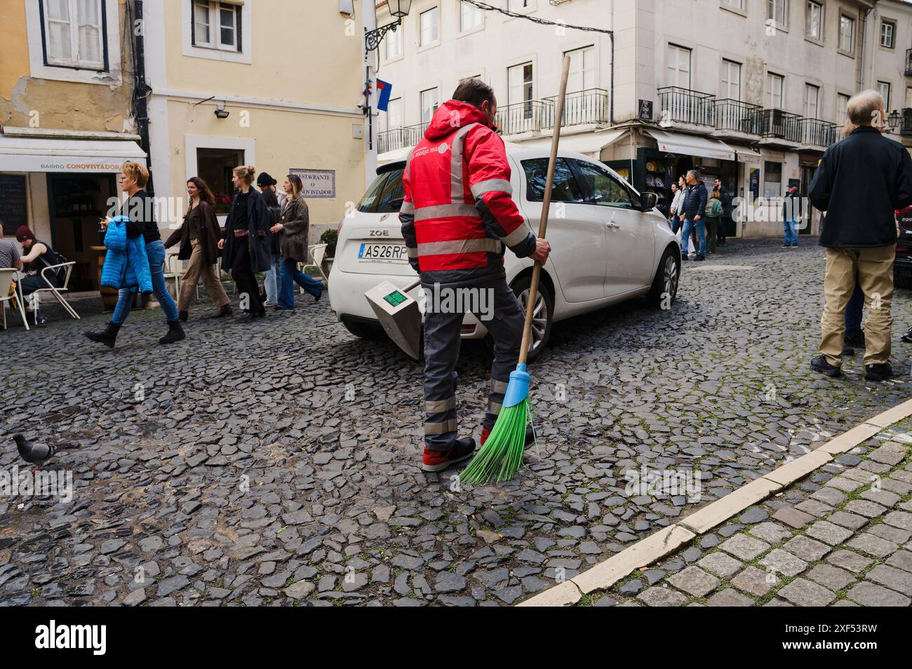 Street sweeper in a red uniform with a green broom on a cobblestone ...