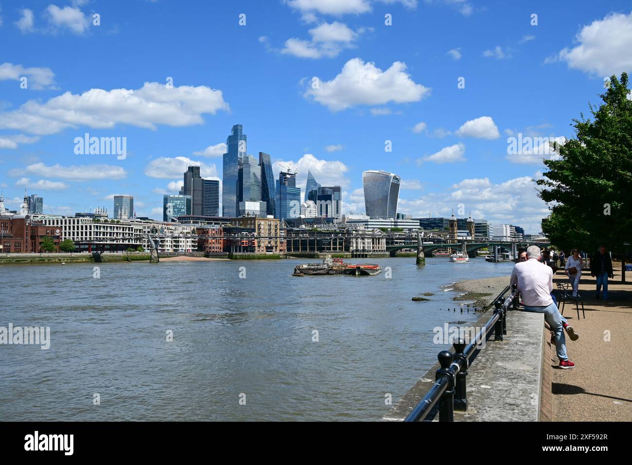 South bank view of the River Thames with moored barges and the city ...