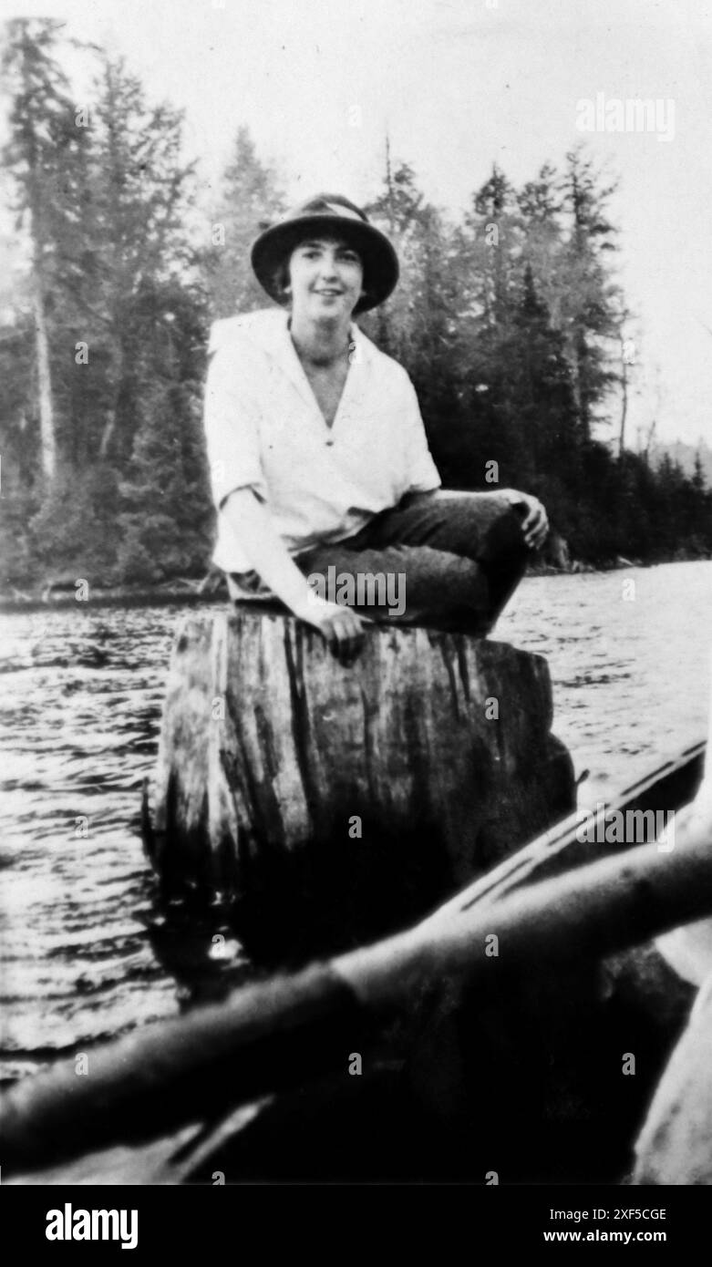 A lady in a hat sitting on a structure surrounded by water, snapshot ...