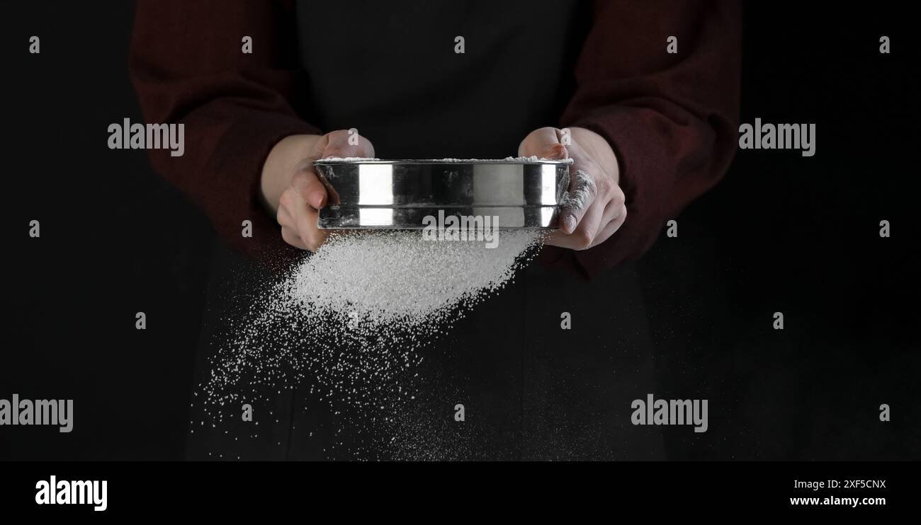 Woman sieving flour at table against black background, closeup Stock ...