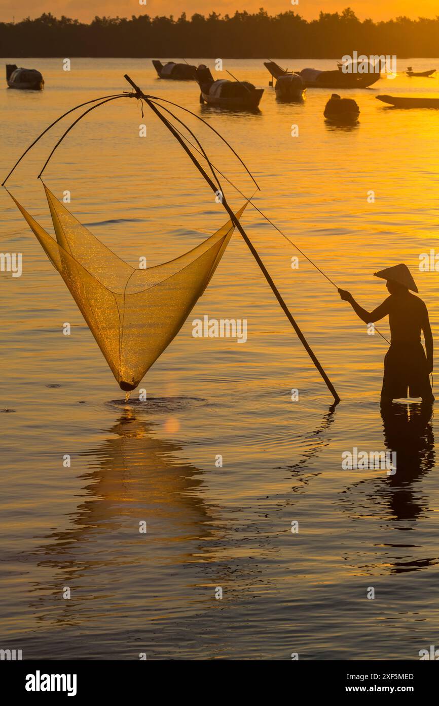 Vietnamese fisherman with traditional fishing net at sunrise on Quang ...