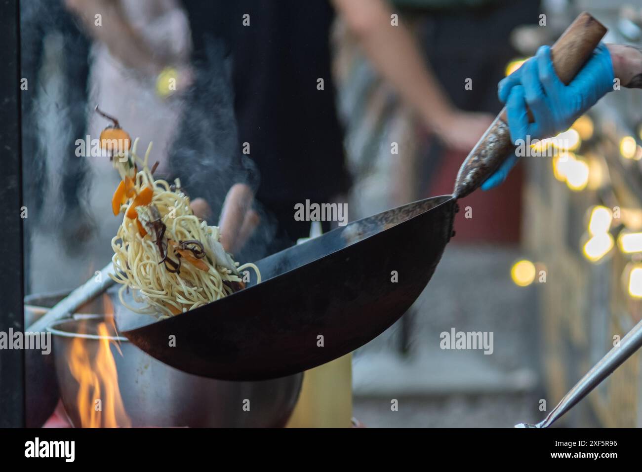 street food vendor stir-frying noodles in a wok over an open flame ...