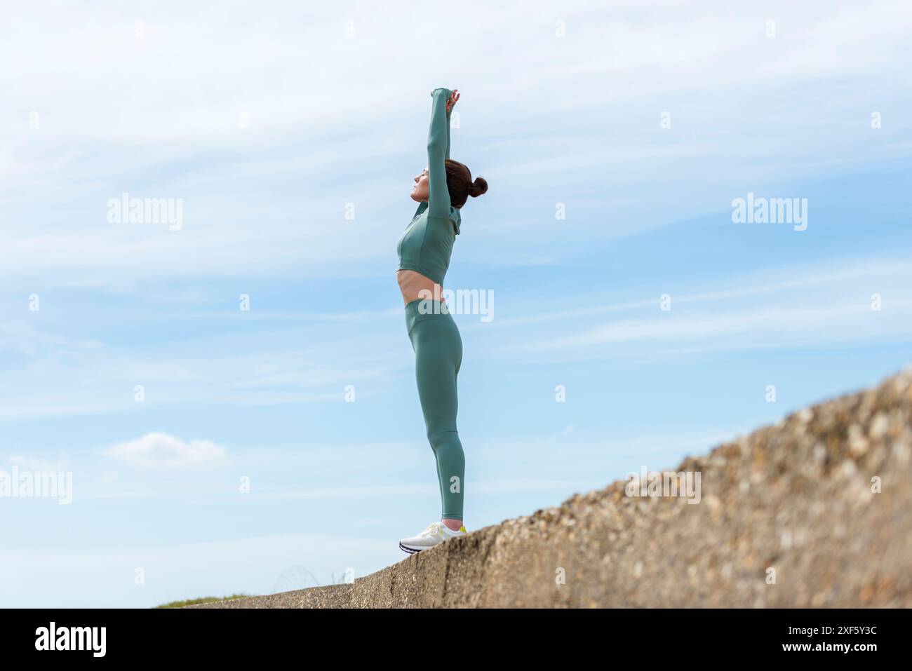 Sporty woman doing arm stretching exercise outdoors against a blue sky ...