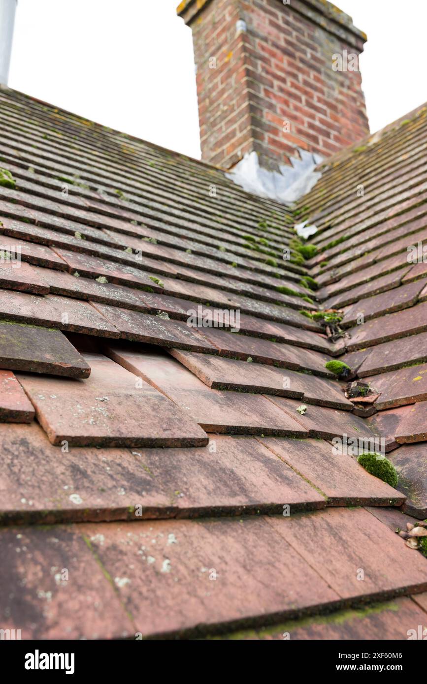 Missing and slipped plain clay roof tiles on a pitched roof of an old ...
