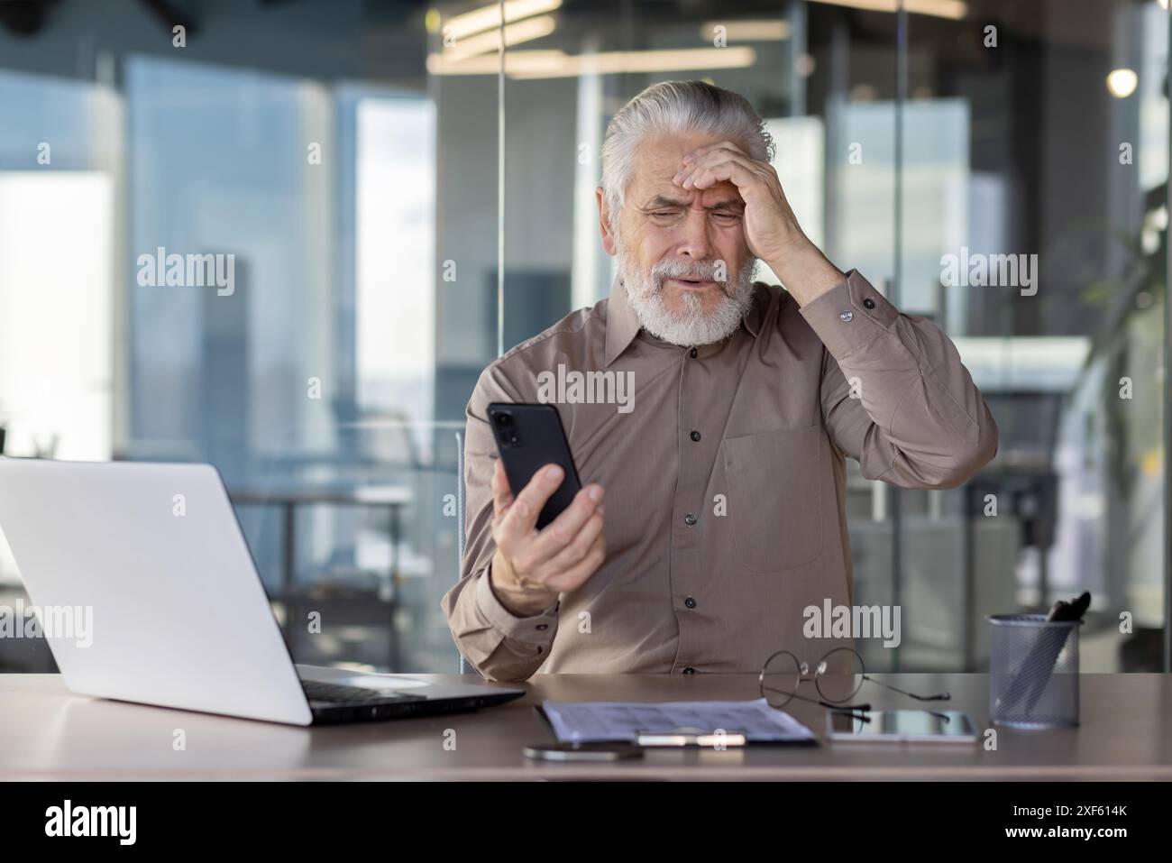 Senior businessman looking at his smartphone with frustration while ...