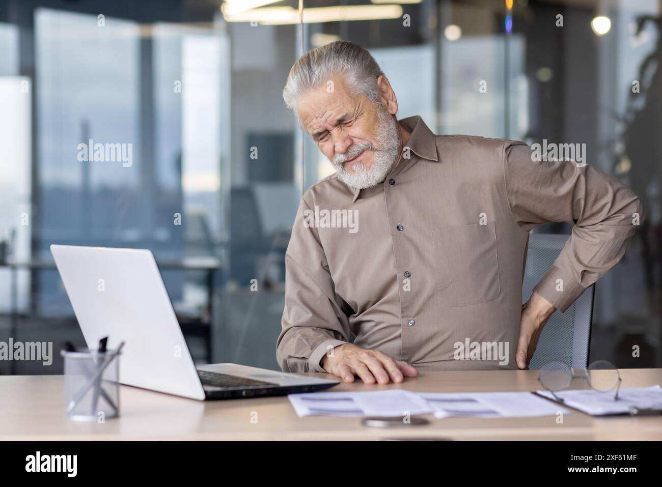 Senior man suffering from back pain while sitting at his office desk ...