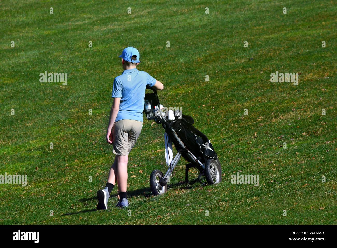 Young teen awaits his turn during a golf tournament. He is standing ...
