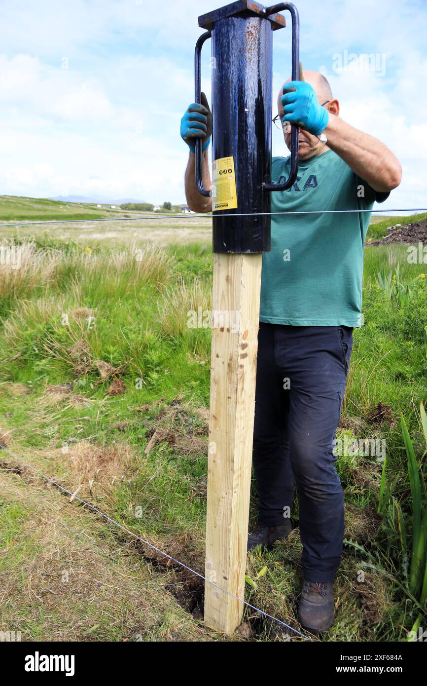 Man using a fence post thumper whilst erecting a fence Stock Photo - Alamy