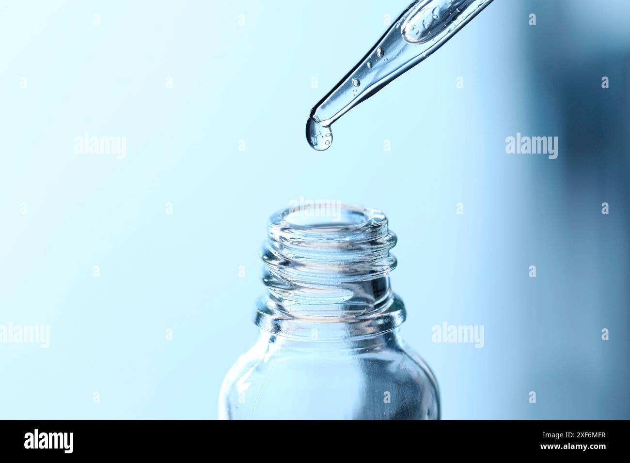 Dripping liquid from pipette into glass bottle on light blue background ...