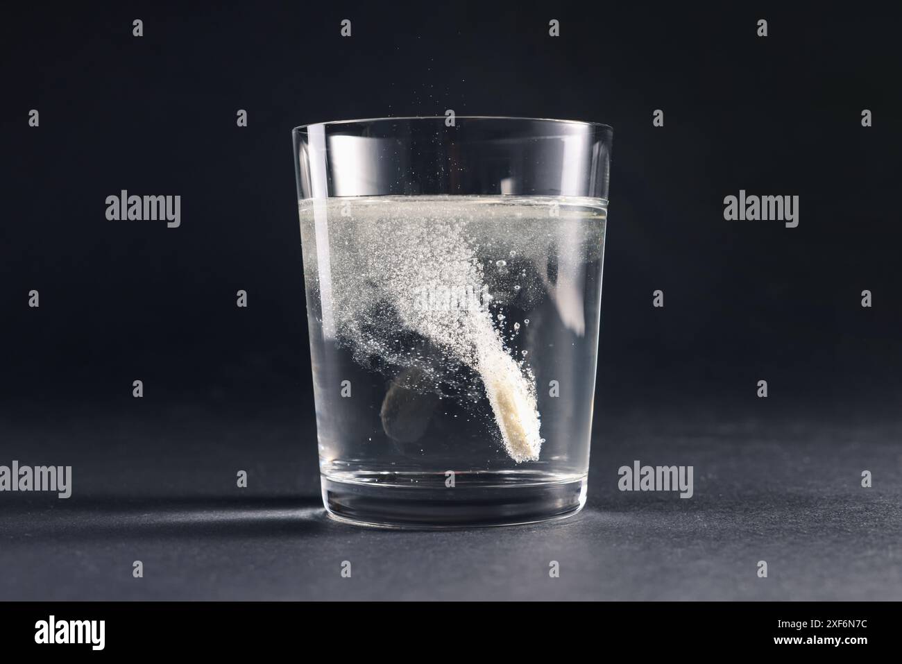 Effervescent pill dissolving in glass of water on grey table Stock Photo - Alamy