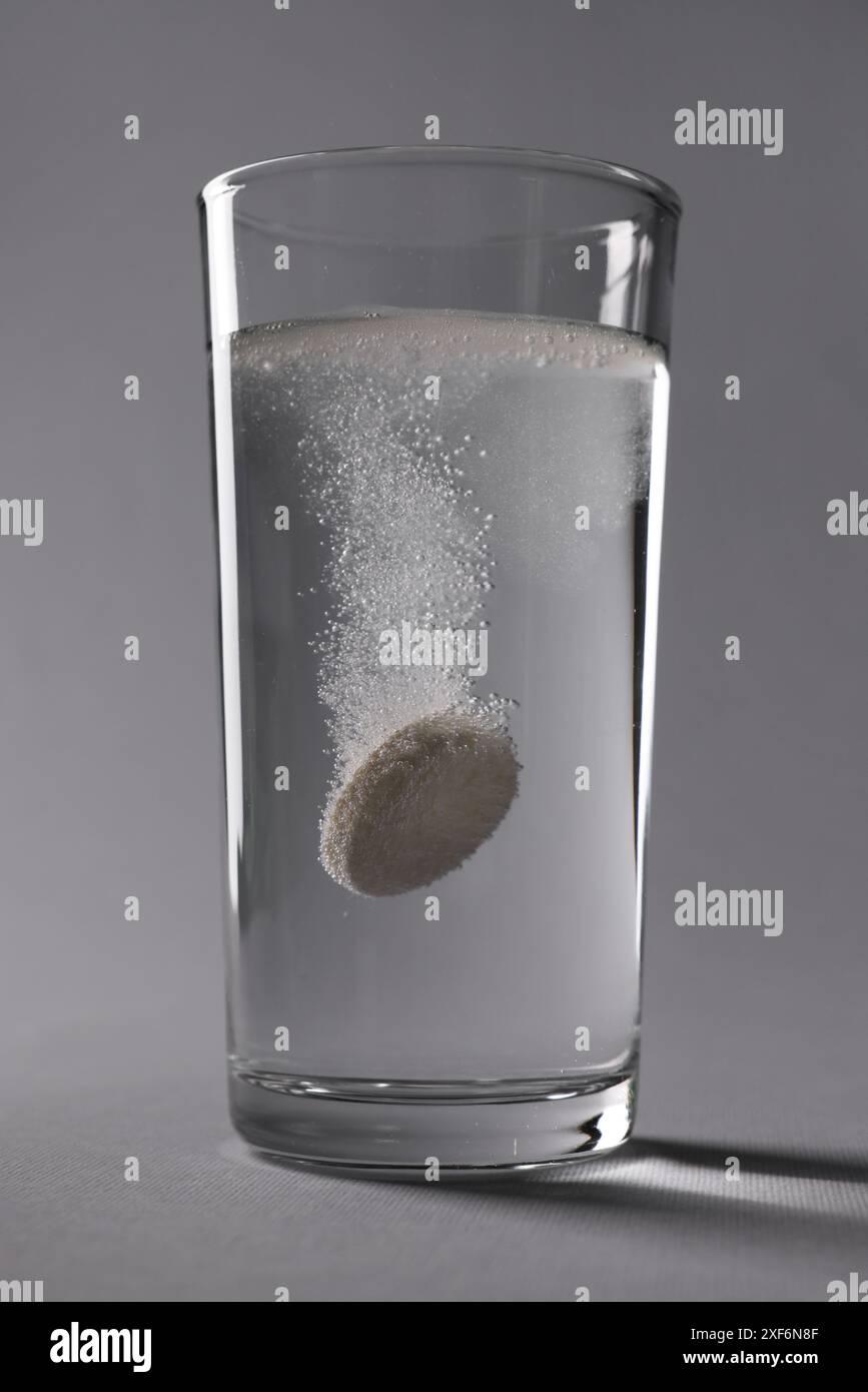 Effervescent pill dissolving in glass of water on grey background Stock ...