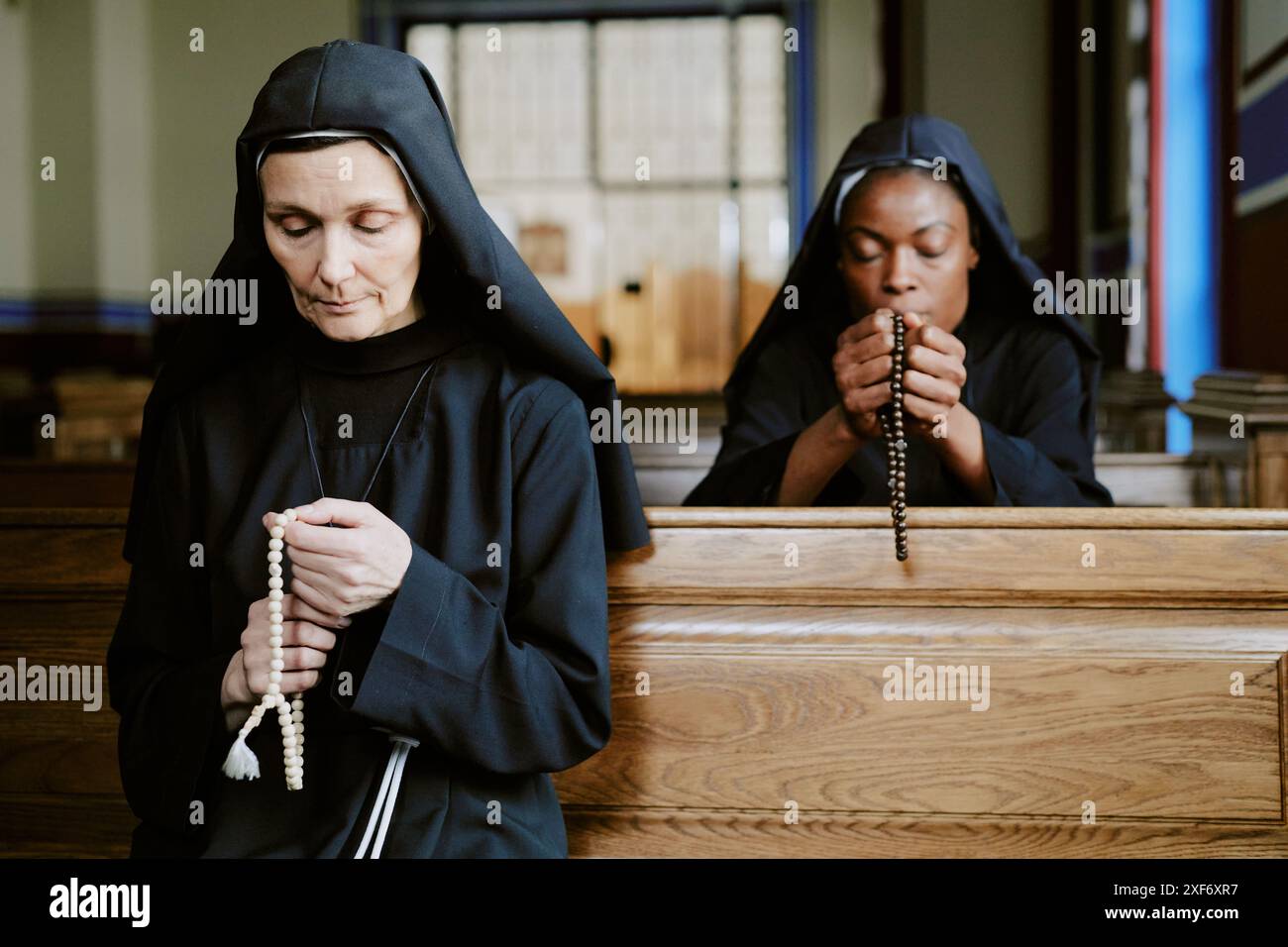 Two ethnically diverse young and mature Catholic nuns sitting on pews ...