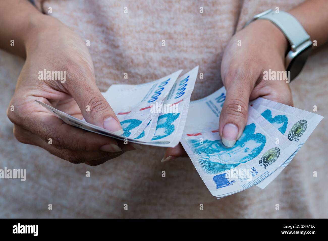 Front photo of a woman's hands counting 10,000 Argentine peso bills ...