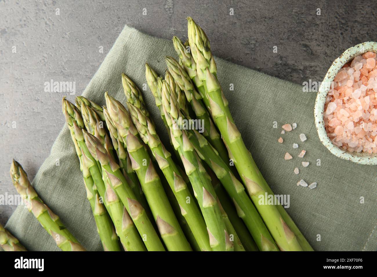 Fresh green asparagus stems and sea salt on grey textured table, top ...