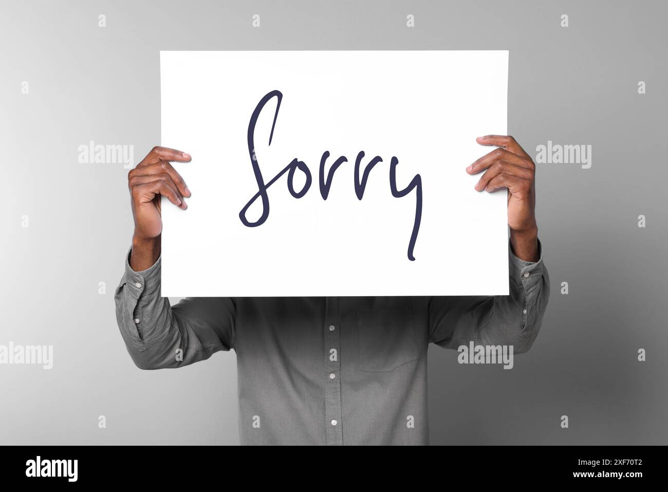 Man hiding face behind card with word Sorry on grey background Stock ...
