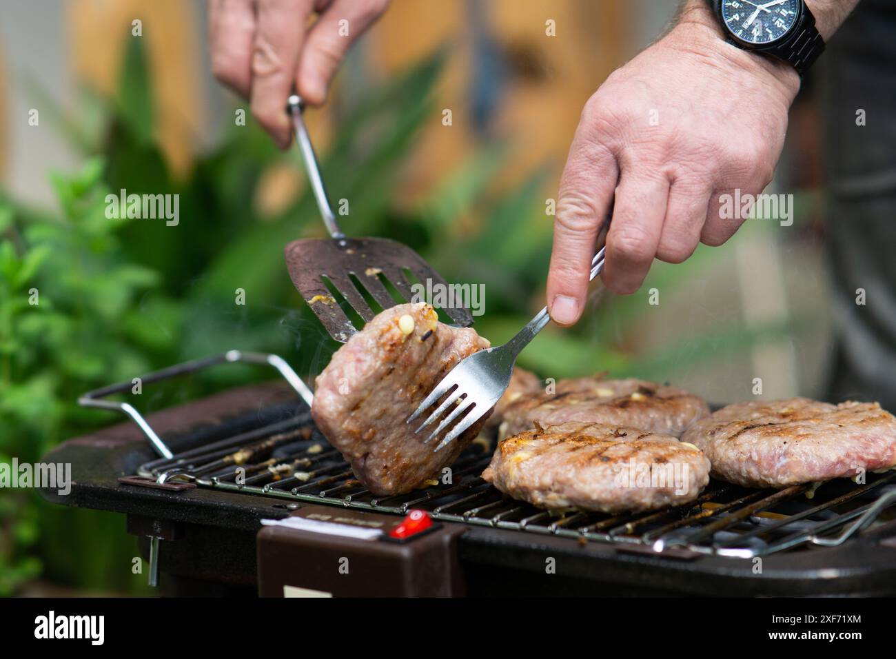 Man grilling burger meat on barbecue grill close up, smoke coming out ...