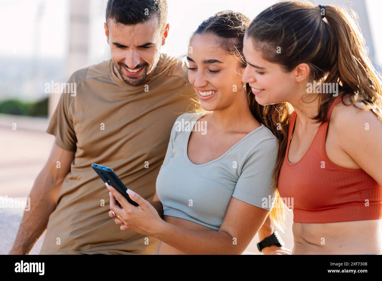 Three young sportive friends using mobile phone after workout routine ...
