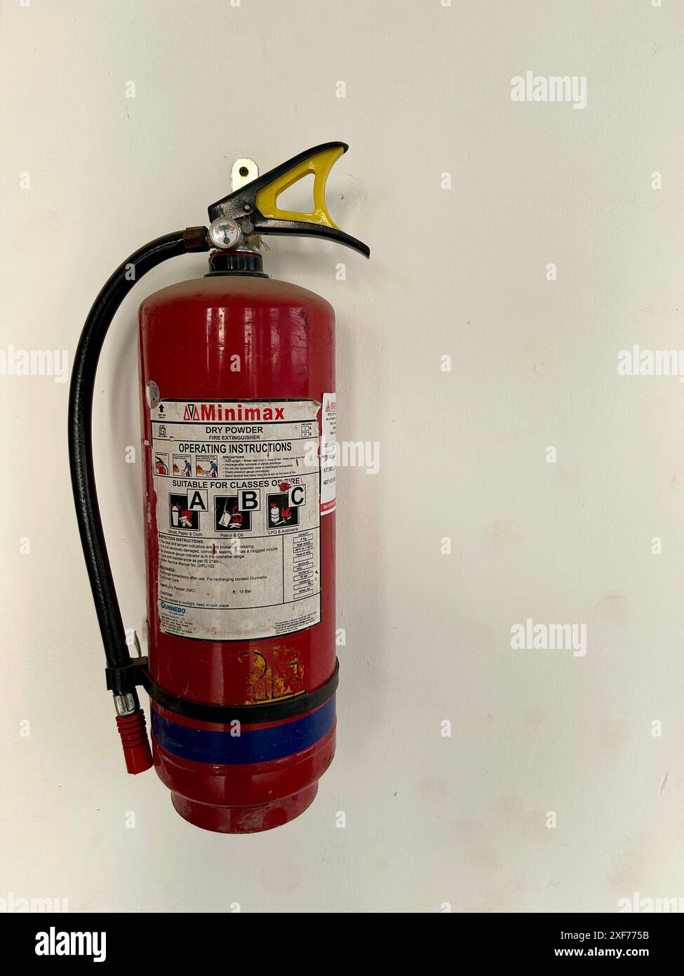 A red dry powder fire extinguisher mounted on a white wall with ...
