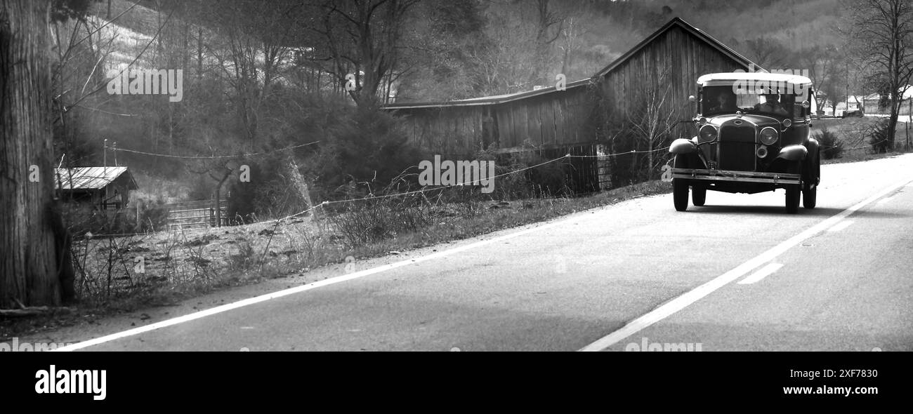 Black and white image, shows old Model T ambling down a country road ...