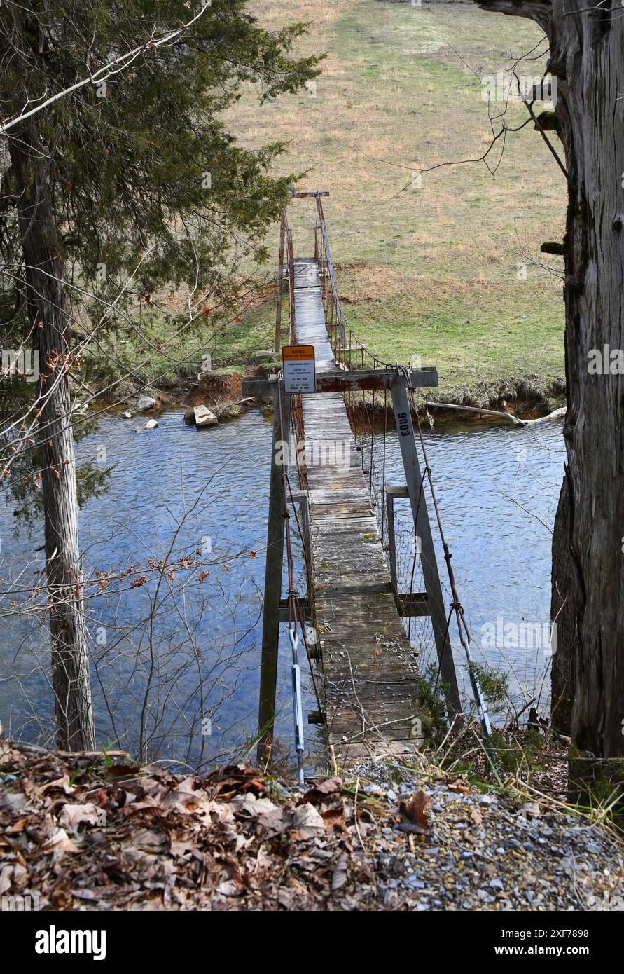 Narrow, swinging, pedestrian bridge crosses creek. Metal frame with ...