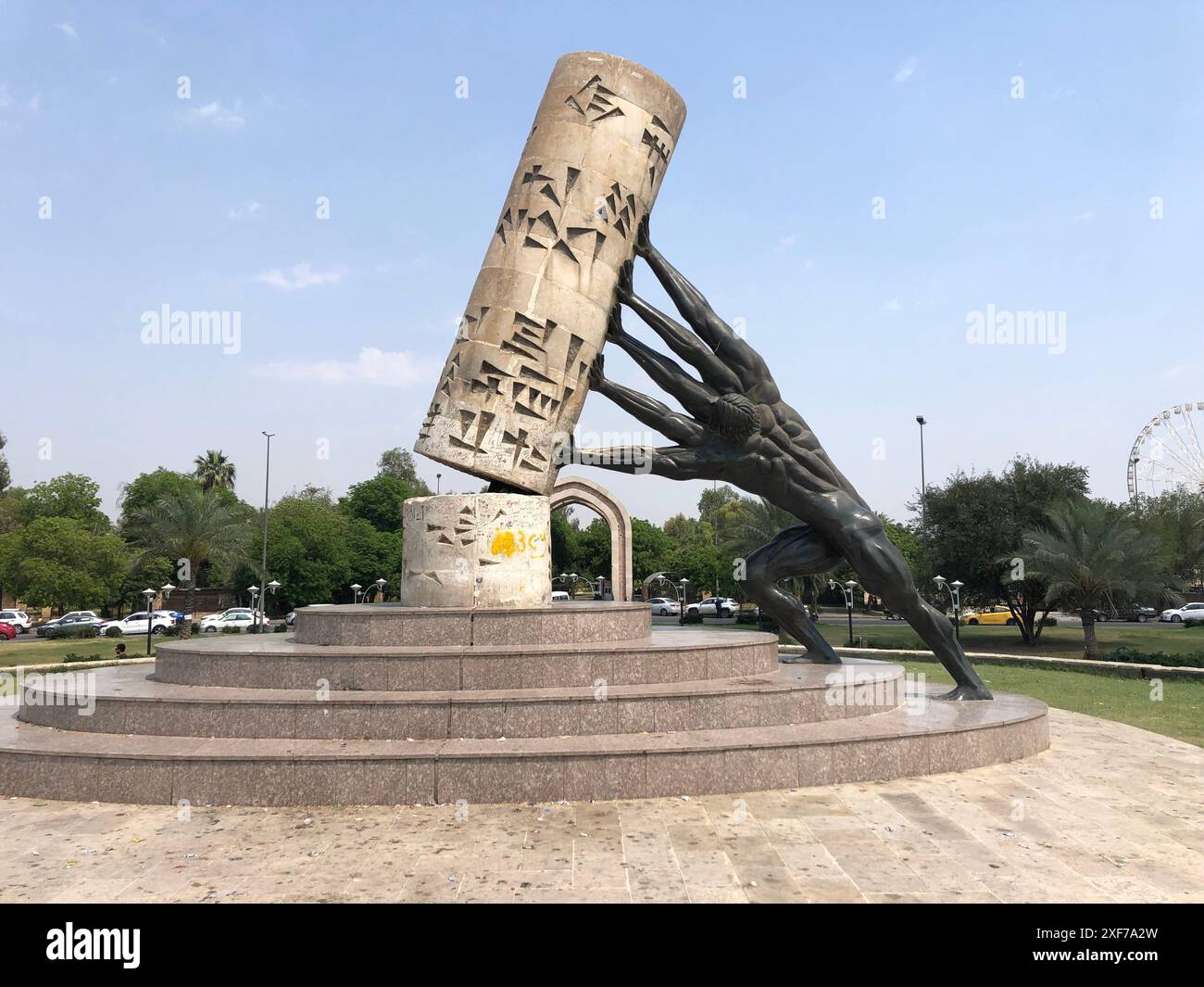 A sculpture of a man pushing a large stone cylinder in a park with ...