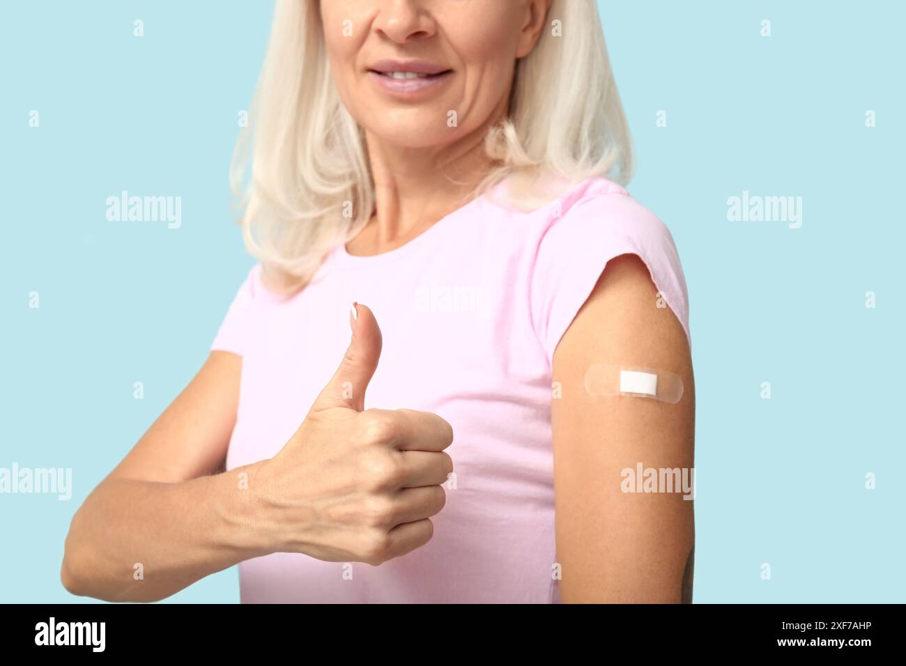 Mature woman with medical patch on arm showing thumb-up against blue ...