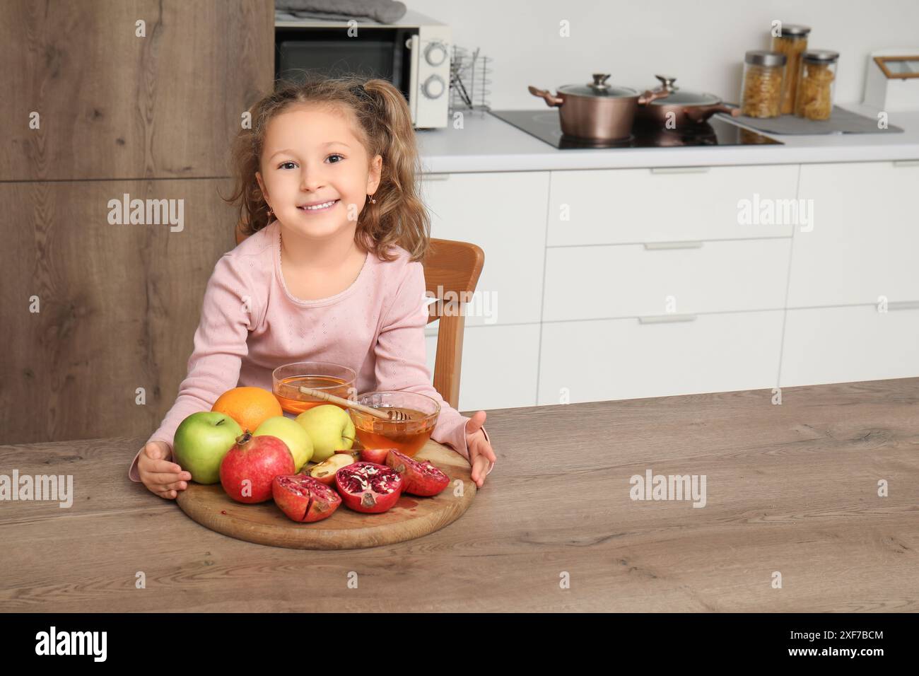 Cute little girl with ripe fruits and honey in kitchen. Rosh Hashanah ...