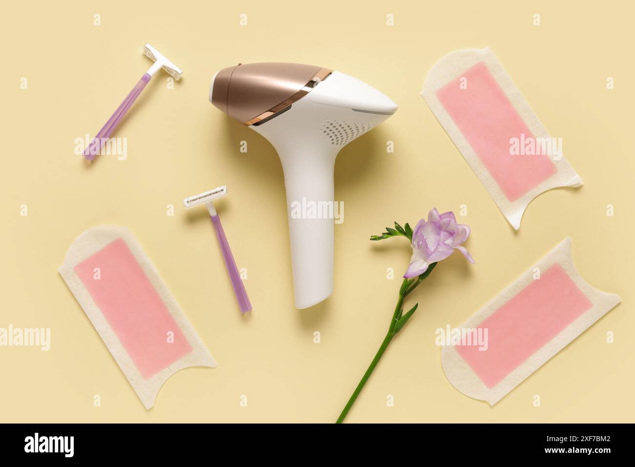 Modern photoepilator with wax strips, razors and flower on yellow ...