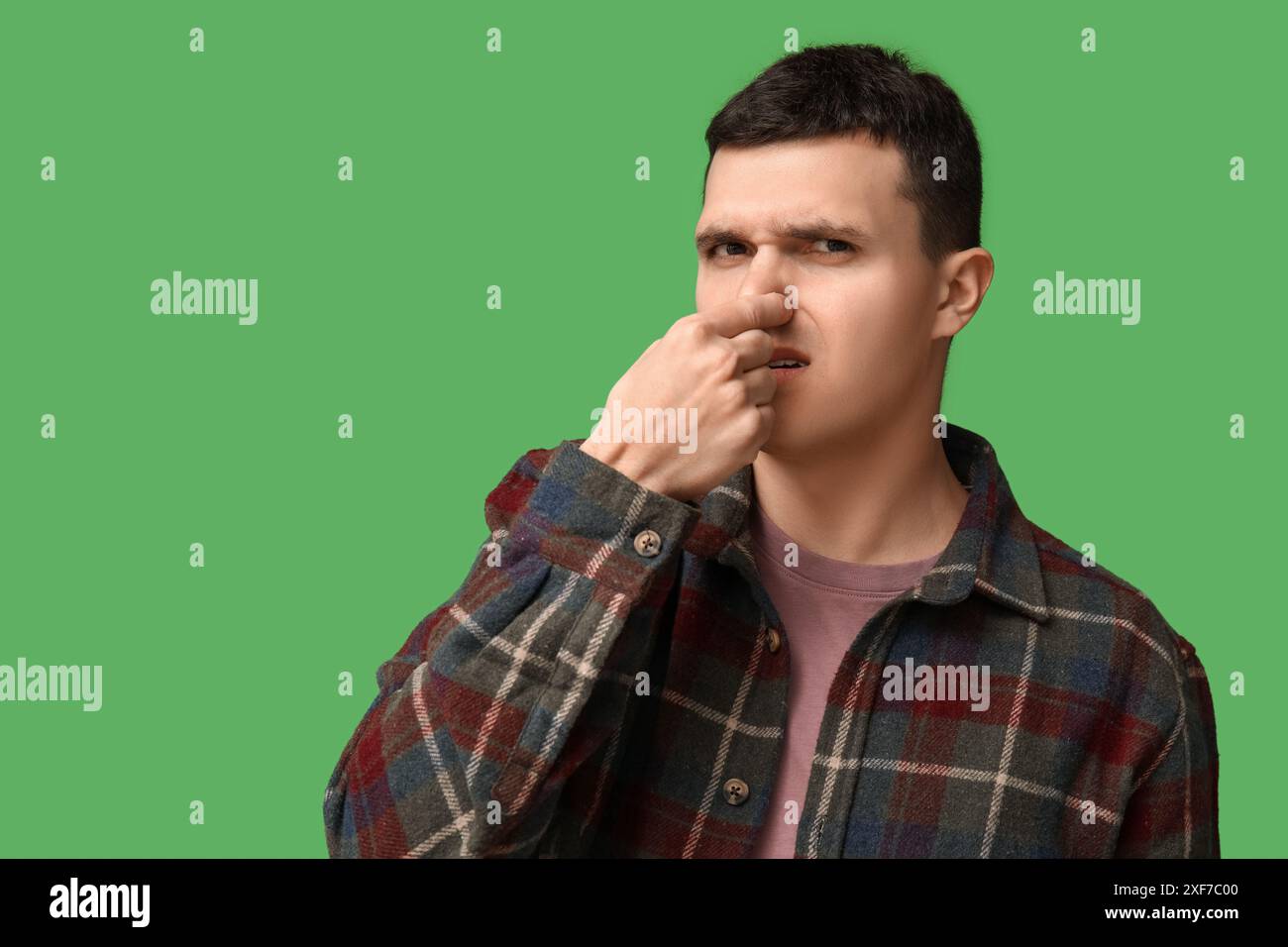 Handsome young man pinching nose because of bad smell on green ...