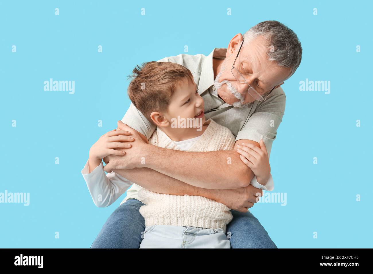 Grandfather hugging his happy cute little grandson hugging on blue ...
