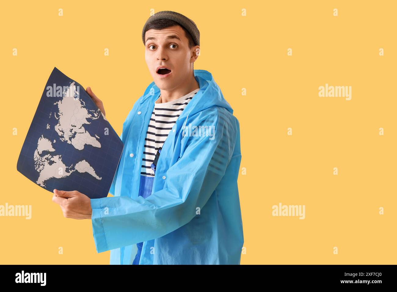 Shocked young sailor in raincoat with world map on yellow background ...