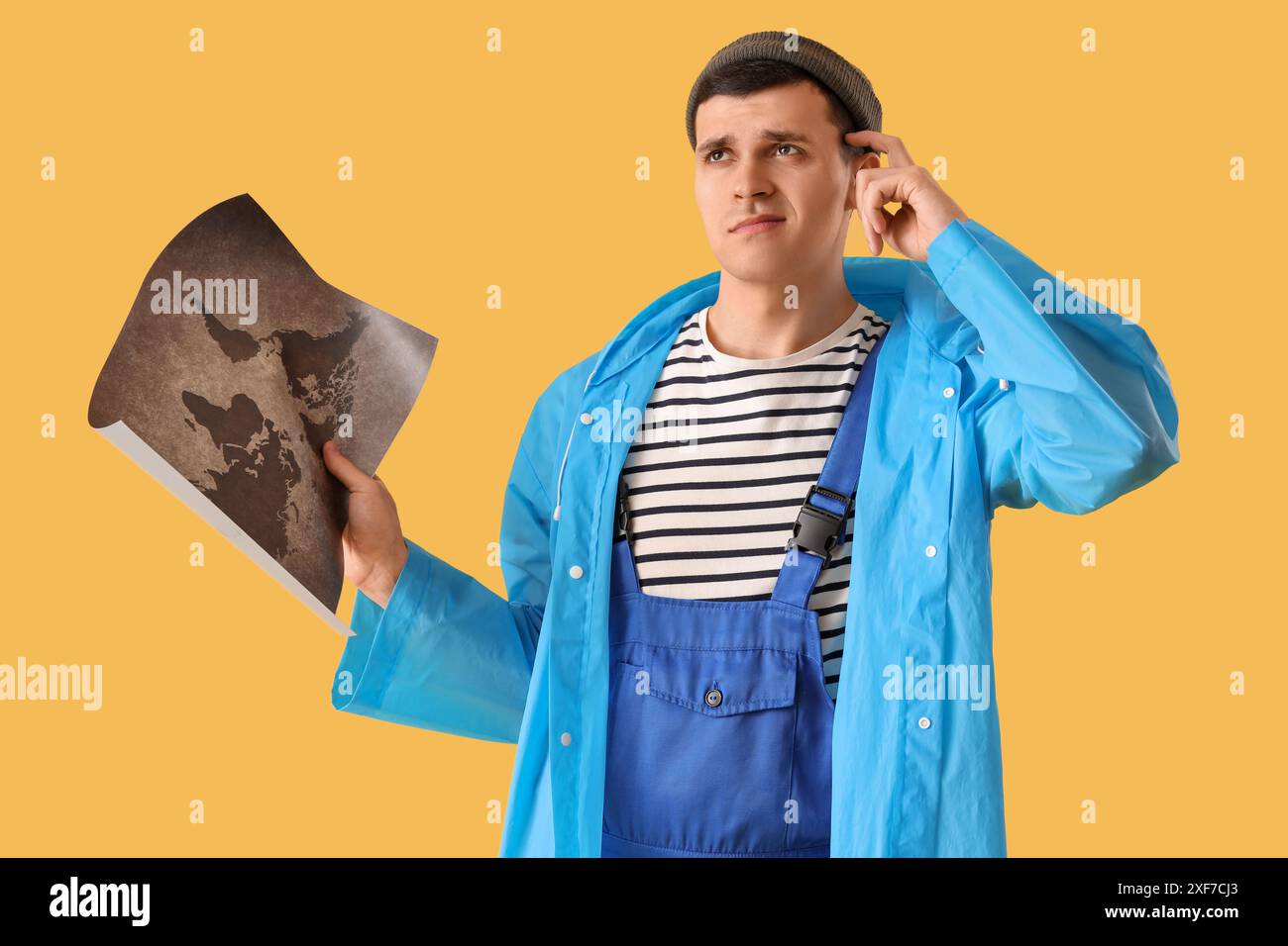 Thoughtful young sailor in raincoat with world map on yellow background ...