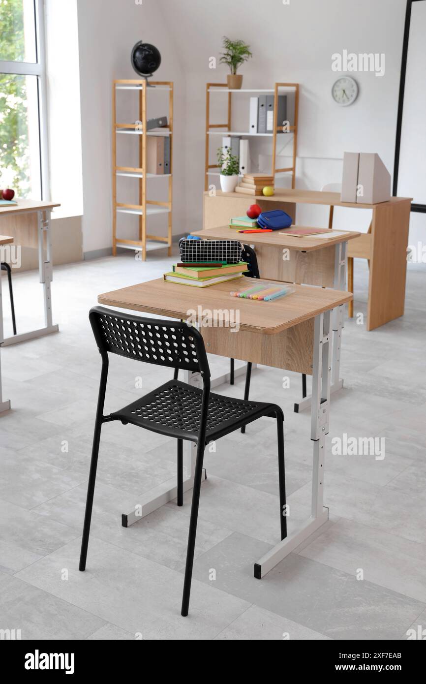 Interior of light classroom with desks, teacher's table and shelf units ...