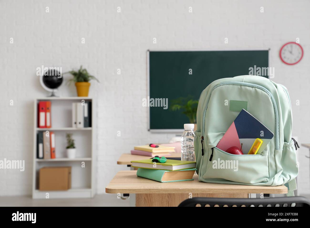 Backpack with books and bottle of water on desk in classroom Stock ...