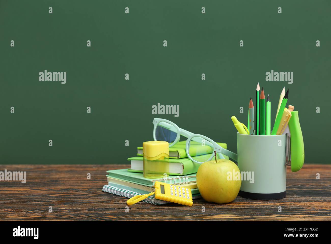 Eyeglasses, different school supplies and apple on table against green ...